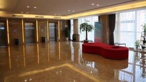 Um hall amplo com piso lustroso, área de estar vermelha e grandes janelas que permitem entrada de luz natural.