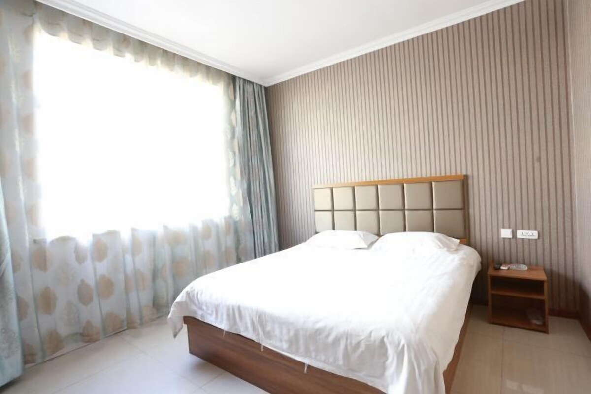 Quarto moderno com cama grande, mesa de cabeceira e janela com cortinas.