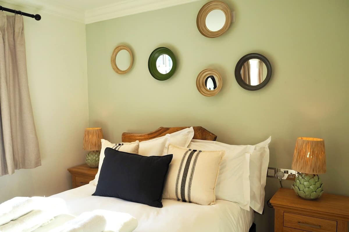 Cama bem arrumada com almofadas brancas e pretas, cabeceira de madeira e duas mesas de cabeceira com luminárias.