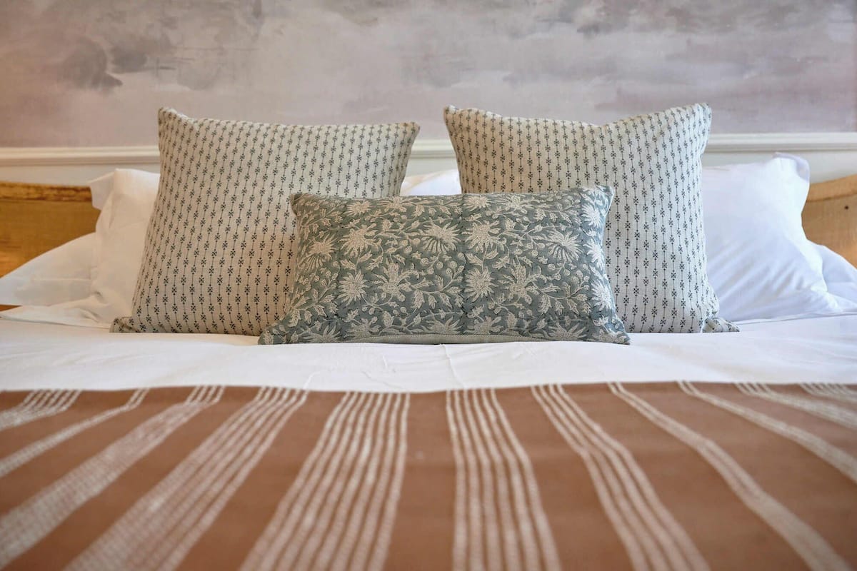 Uma cama com roupa de cama listrada, dois travesseiros com padrão floral e um travesseiro liso.
