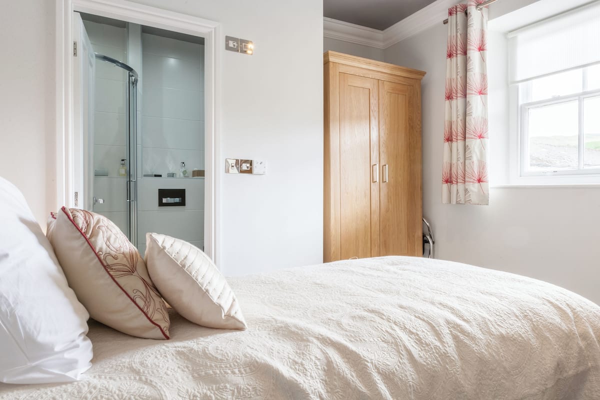 Quarto com cama, guarda-roupa, área de chuveiro e janela com cortinas.