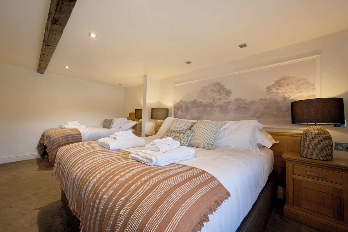 Quarto de hotel com duas camas, um grande mural na parede, uma televisão de tela plana e uma mesinha de cabeceira de madeira.