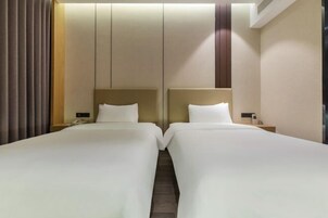 Quarto de hotel com duas camas, piso de madeira e design moderno.