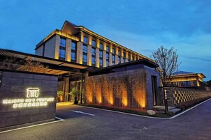 Um hotel moderno com entrada ampla, fachada bem iluminada e área ajardinada com árvores.