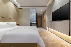 Quarto de hotel moderno com uma cama grande, televisão de tela plana e vista para a cidade.