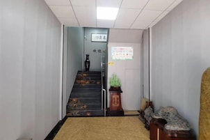 Um corredor com escadas, uma mesa de recepção e um mural de avisos.