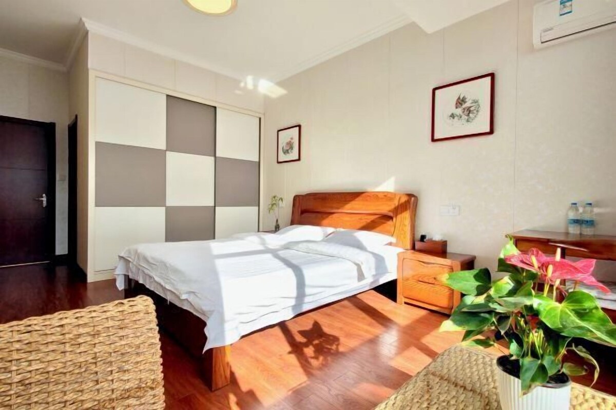 Quarto com cama, piso de madeira, mesa de cabeceira, cômoda e um vaso de planta.