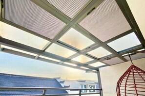Quarto com claraboia, cadeira suspensa e vista para edifícios tradicionais.