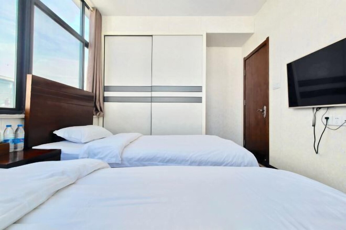 Quarto de hotel com duas camas, uma televisão na parede e uma janela com cortinas.