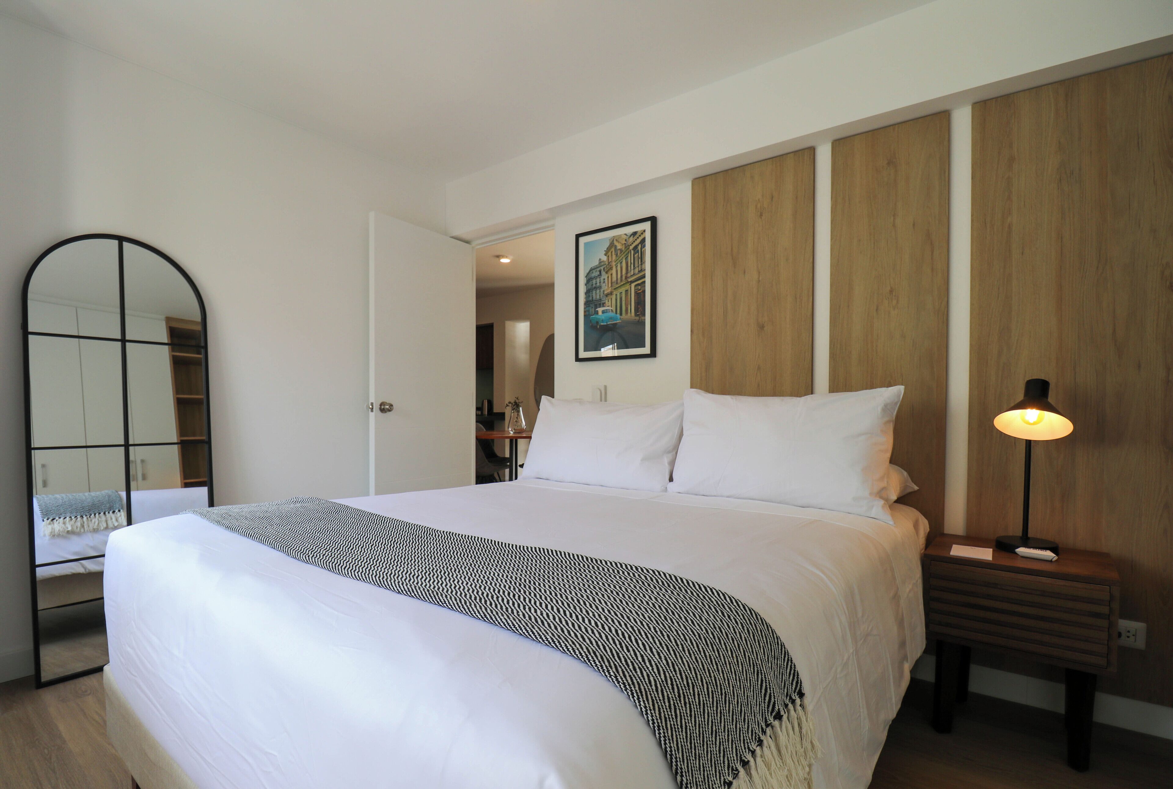 Cama bem arrumada com manta estampada, luminária de cabeceira e parede de painéis de madeira.
