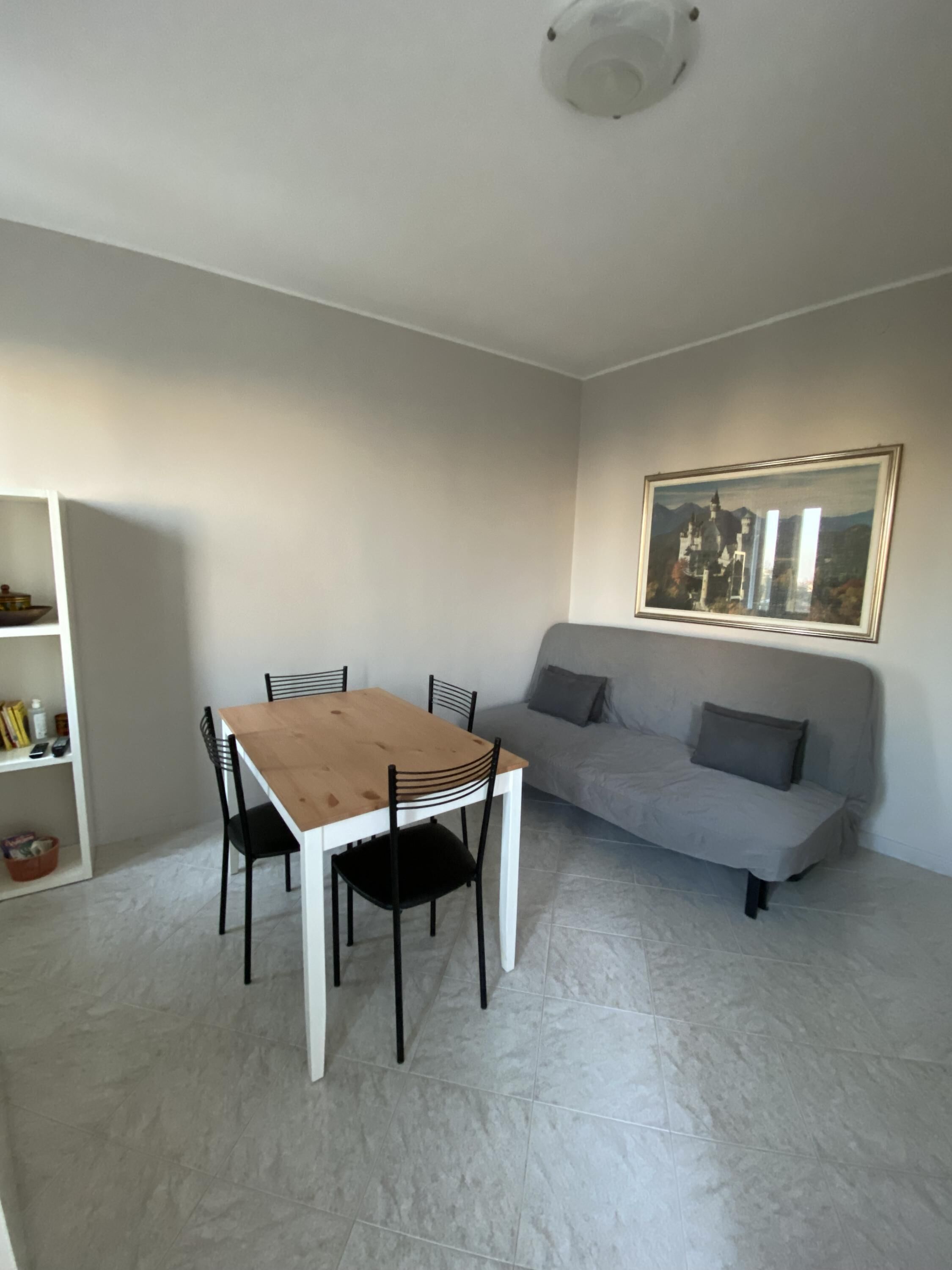 Uma sala de estar moderna com uma mesa de jantar, cadeiras, sofá e estante de livros.
