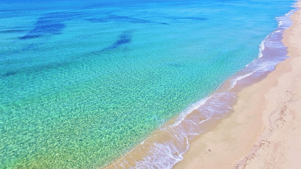Uma praia com águas turquesa cristalinas e uma extensa faixa de areia.
