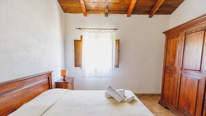Quarto com cama de madeira, mesa de cabeceira com abajur, guarda-roupa e janela com cortinas.