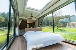 Quarto moderno com claraboia, cama e vista para uma paisagem verde.