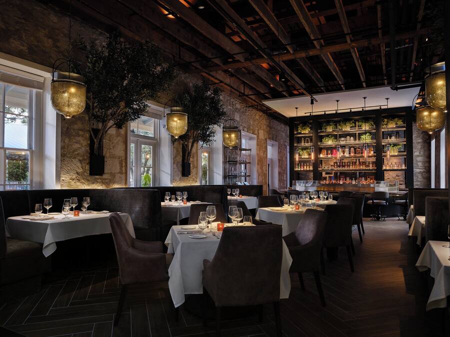 Restaurante com mesas preparadas para refeições, área de bar com prateleiras de garrafas e parede com árvore e estantes.