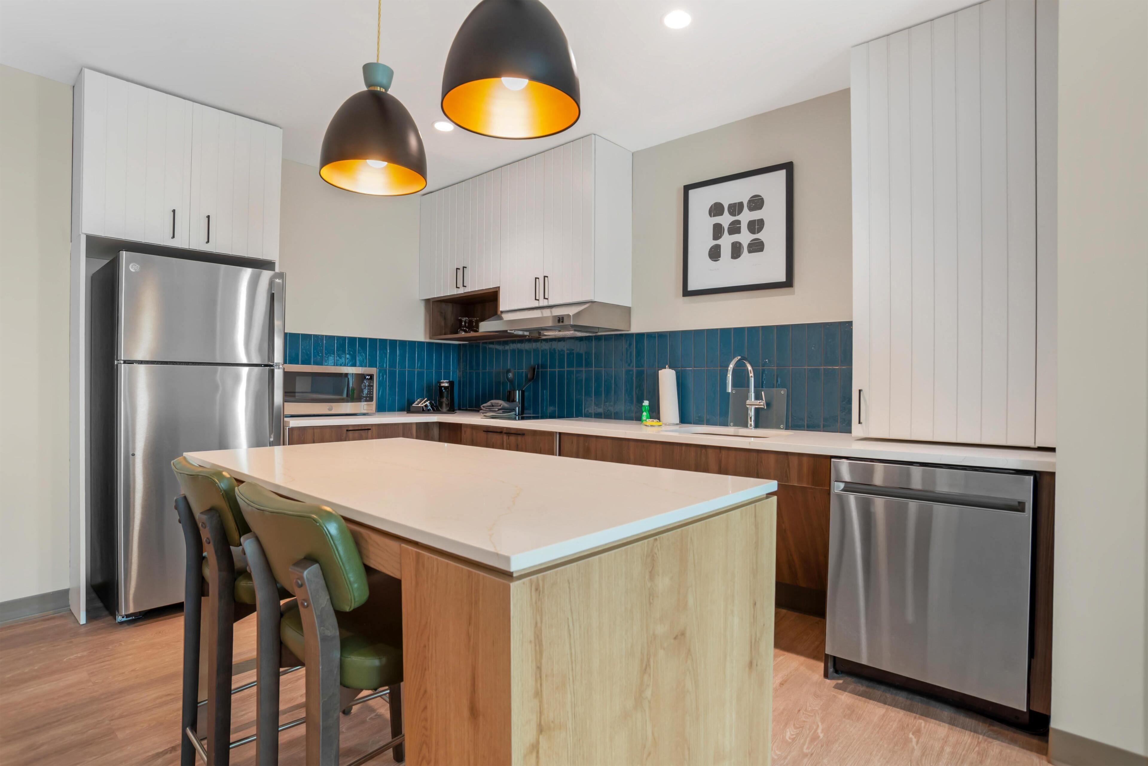 Uma cozinha moderna com ilha central, eletrodomésticos de aço inoxidável e iluminação pendente.