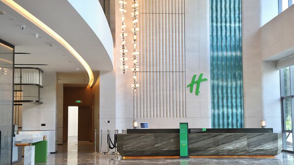 Uma área de recepção de hotel moderna com um balcão de mármore, luminárias verticais e um grande letreiro em formato de 'H' na parede.