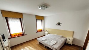 Quarto com cama, mesas de cabeceira, escrivaninha e uma cadeira.