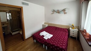 Quarto com cama, mesa de cabeceira, luminária, chuveiro e um objeto decorativo na parede.