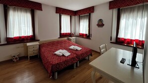 Quarto com uma cama grande, duas mesas de cabeceira, uma escrivaninha e uma cadeira.