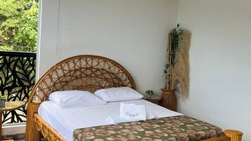 Quarto com cama, ventilador de teto, janela com persianas, planta em vaso e um objeto decorativo na parede.
