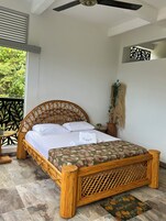 Quarto com cama, ventilador de teto, janela com persianas, planta em vaso e um objeto decorativo na parede.