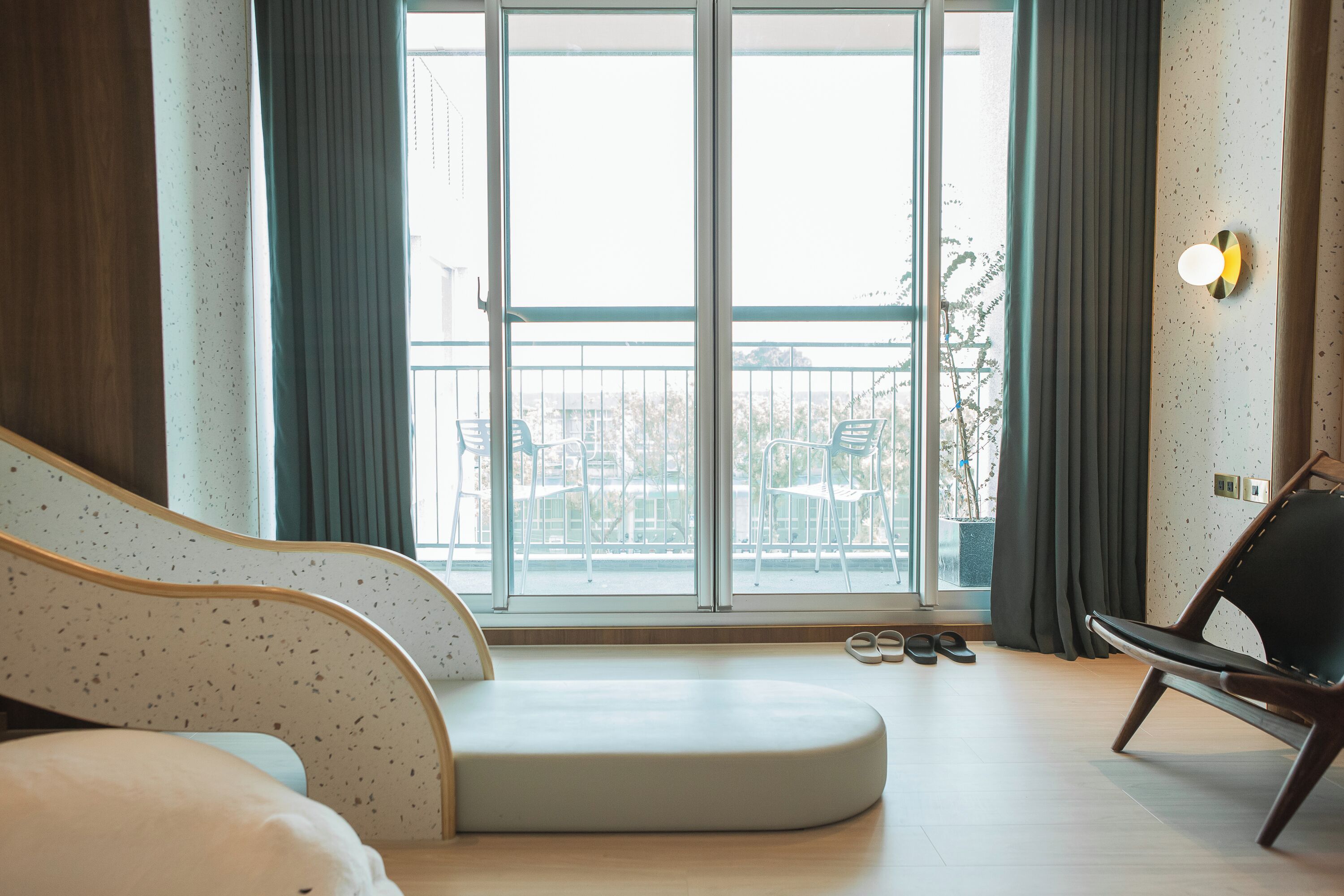 Quarto moderno com uma janela grande, um sofá, uma cadeira e um par de chinelos no chão.