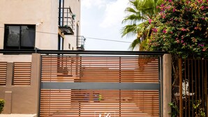 Um edifício moderno com um grande portão de madeira, uma varanda e uma palmeira.