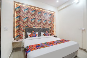 Uma cama bem arrumada com colcha de padrão geométrico, cabeceira estofada cinza e parede colorida com padrão em zigue-zague ao fundo.