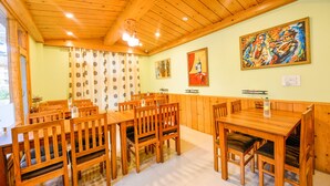 Uma área de refeições com mesas e cadeiras de madeira, uma cortina estampada e um quadro na parede.