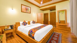 Uma cama com estrutura de madeira e um cobertor colorido, um criado-mudo com uma chaleira e um quadro na parede.