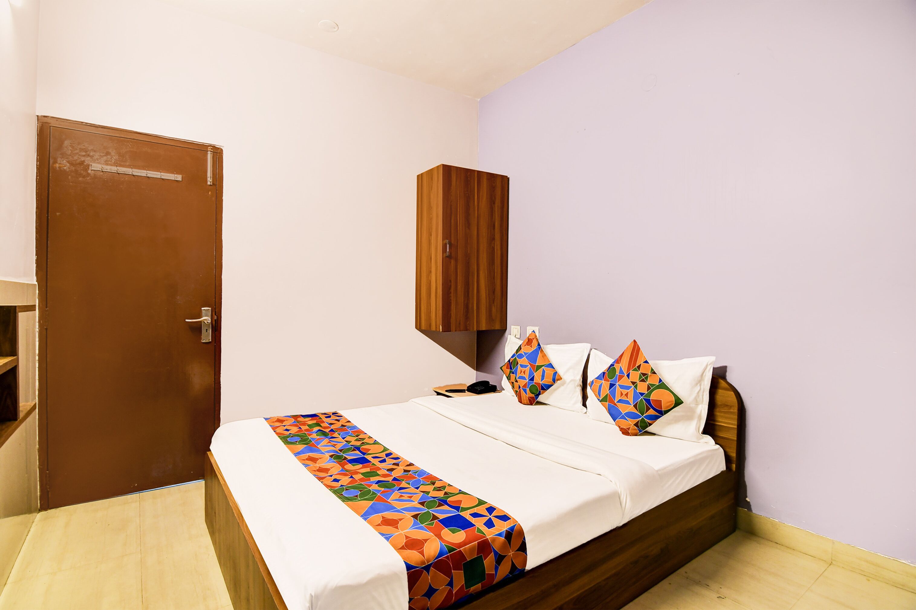 Quarto de hotel com uma cama, um guarda-roupa de madeira e uma porta.