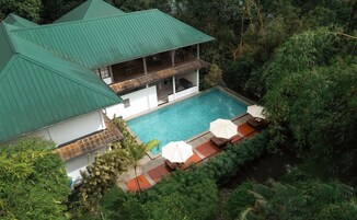 Uma casa de dois andares com piscina, rodeada por vegetação exuberante.