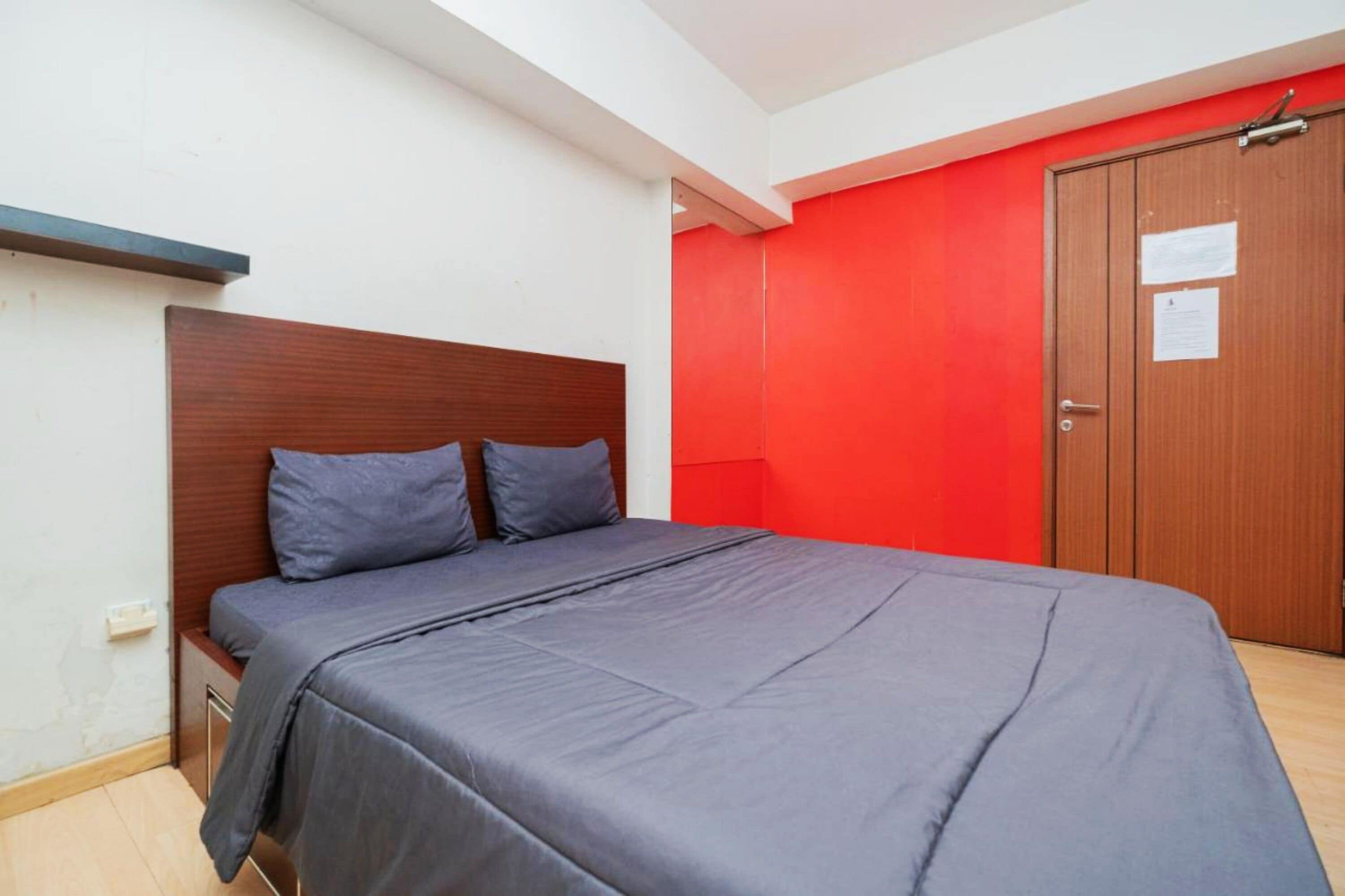 Quarto com cama, cabeceira de madeira, parede de destaque vermelha e uma porta com aviso.