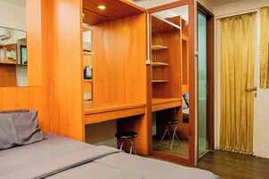 Quarto com cama, guarda-roupa de madeira, espelho e porta com cortinas.