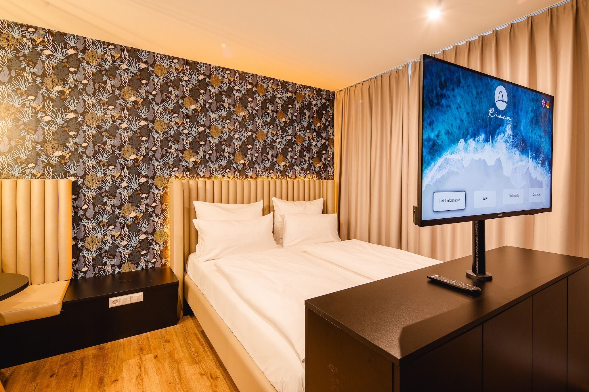 Quarto de hotel com cama, televisão sobre uma escrivaninha e parede estampada.