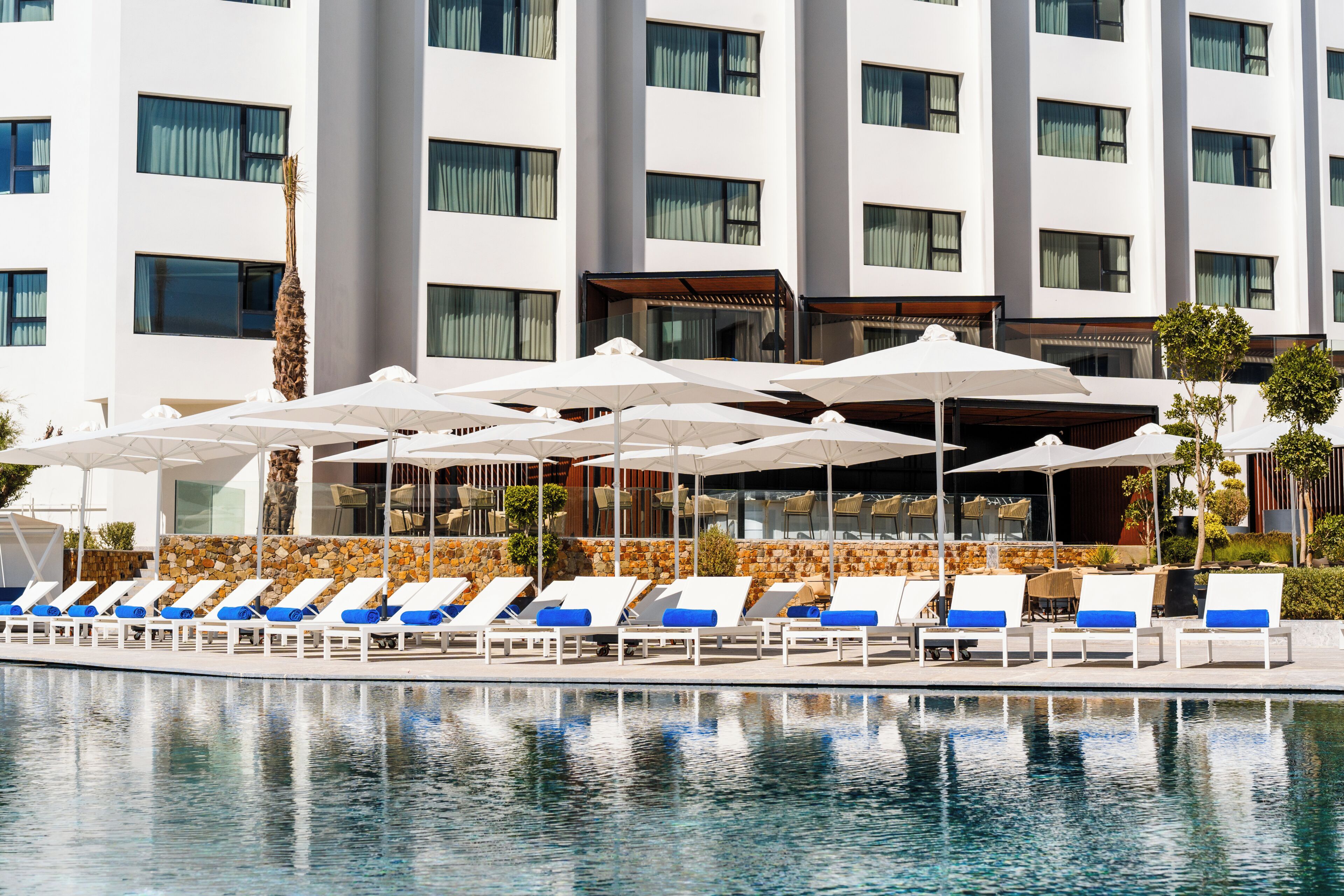 Um hotel com piscina, espreguiçadeiras, guarda-sóis e uma parede de pedra.
