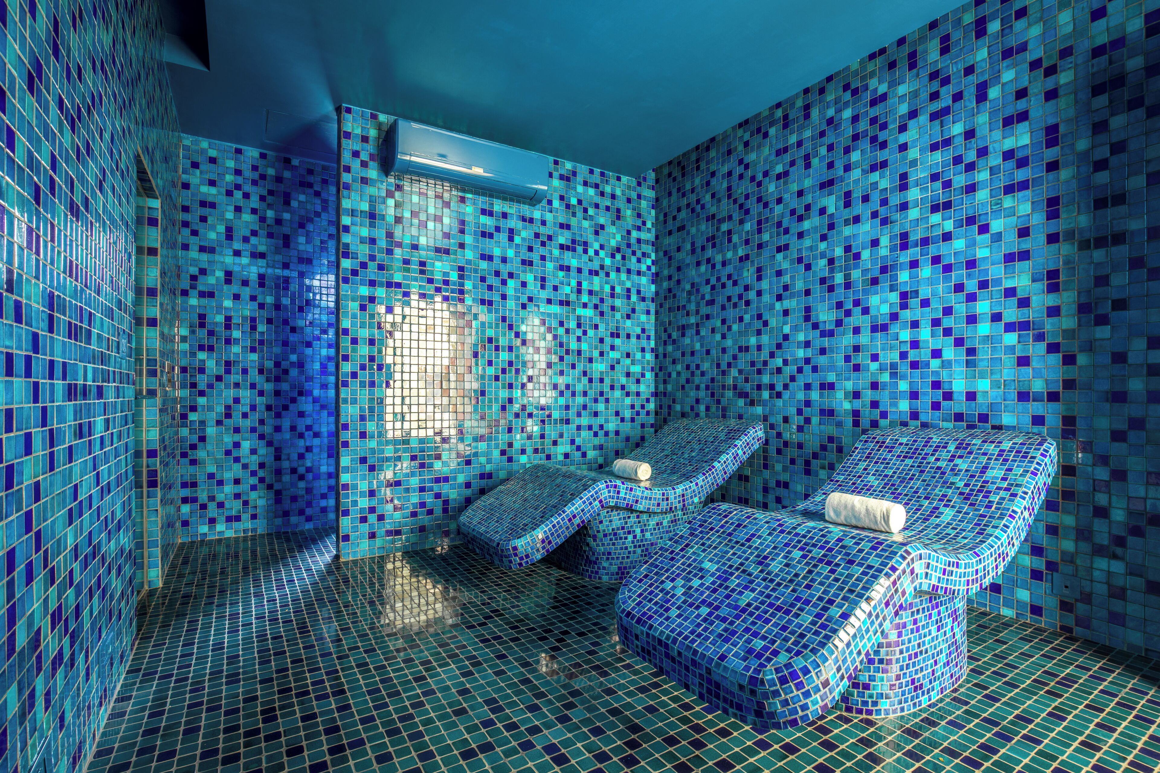 Quarto com paredes e chão em mosaico, duas poltronas reclináveis e uma janela com vista.