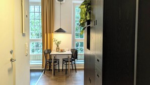 Uma área de refeições com mesa e cadeiras, uma luminária pendente e vista através de amplas janelas.