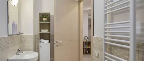 Um banheiro moderno com pia branca, espelho, porta-toalhas e porta de madeira.