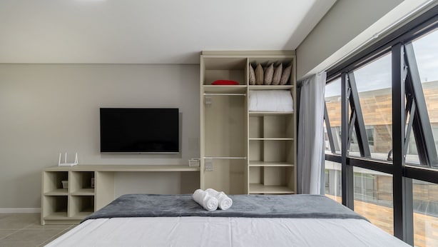 Quarto de hotel moderno com cama, televisão, guarda-roupa e uma grande janela.