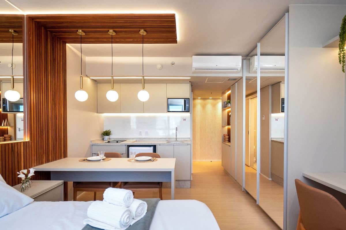 Quarto de hotel moderno com parede de destaque em madeira, área de jantar, cozinha e sala de estar separada.
