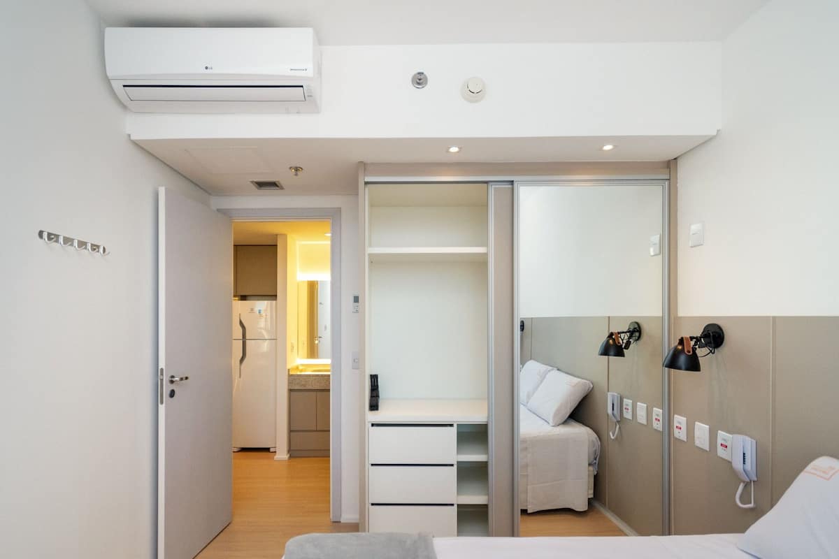 Quarto de hotel com cama, mesa de cabeceira, guarda-roupa, banheiro e ar condicionado.