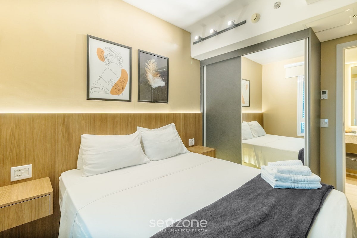 Quarto de hotel com cama, mesa de cabeceira, espelho e obras de arte na parede.