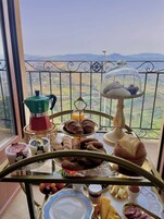 Uma mesa na varanda com diversos alimentos, uma cafeteira e vista para o campo.