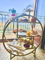 Um carrinho de café da manhã com diversos alimentos e utensílios em uma varanda com vista panorâmica.
