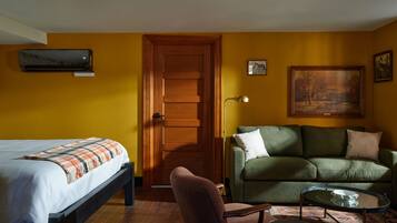 Quarto com cama, sofá verde, poltrona, mesa redonda pequena e um quadro na parede.