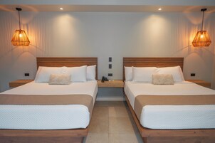 Quarto duplo com duas camas, cada uma com cabeceira de madeira, roupa de cama branca e uma pequena mesa de cabeceira com abajur.