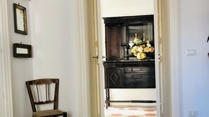 Um corredor com uma cadeira de madeira, um armário de madeira escura com um vaso de flores e um tapete estampado no chão.