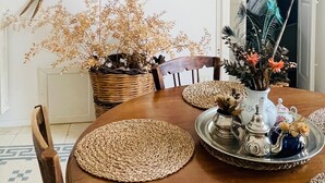 Uma sala de jantar com mesa de madeira, jogos americanos trançados e bandeja decorativa com bules de chá antigos.